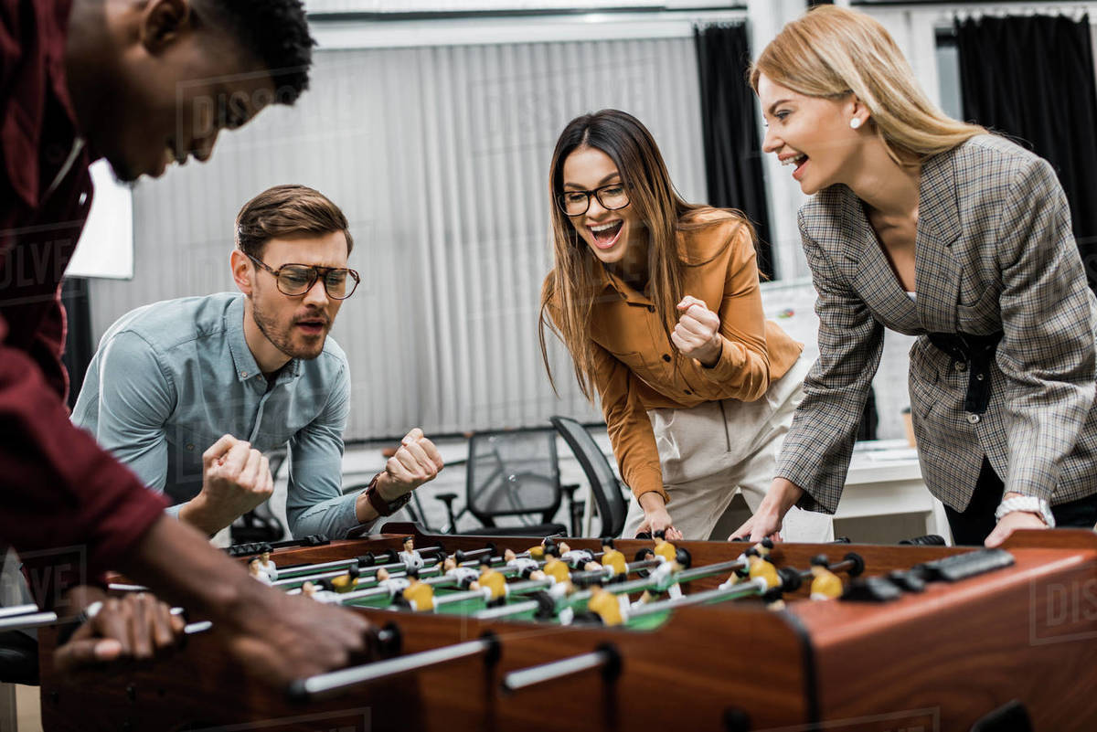 Smiling multicultural business colleagues playing table football ...