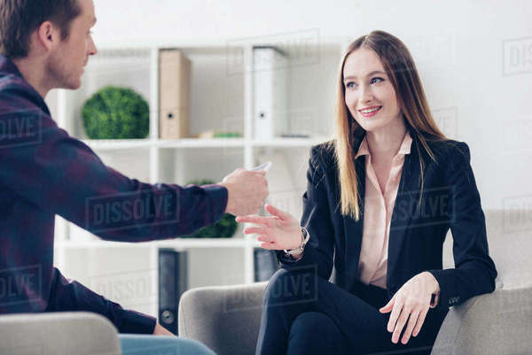 Smiling young businesswoman in suit giving interview to journalist in ...