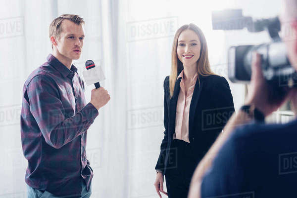 Smiling beautiful businesswoman in suit giving interview to journalist ...