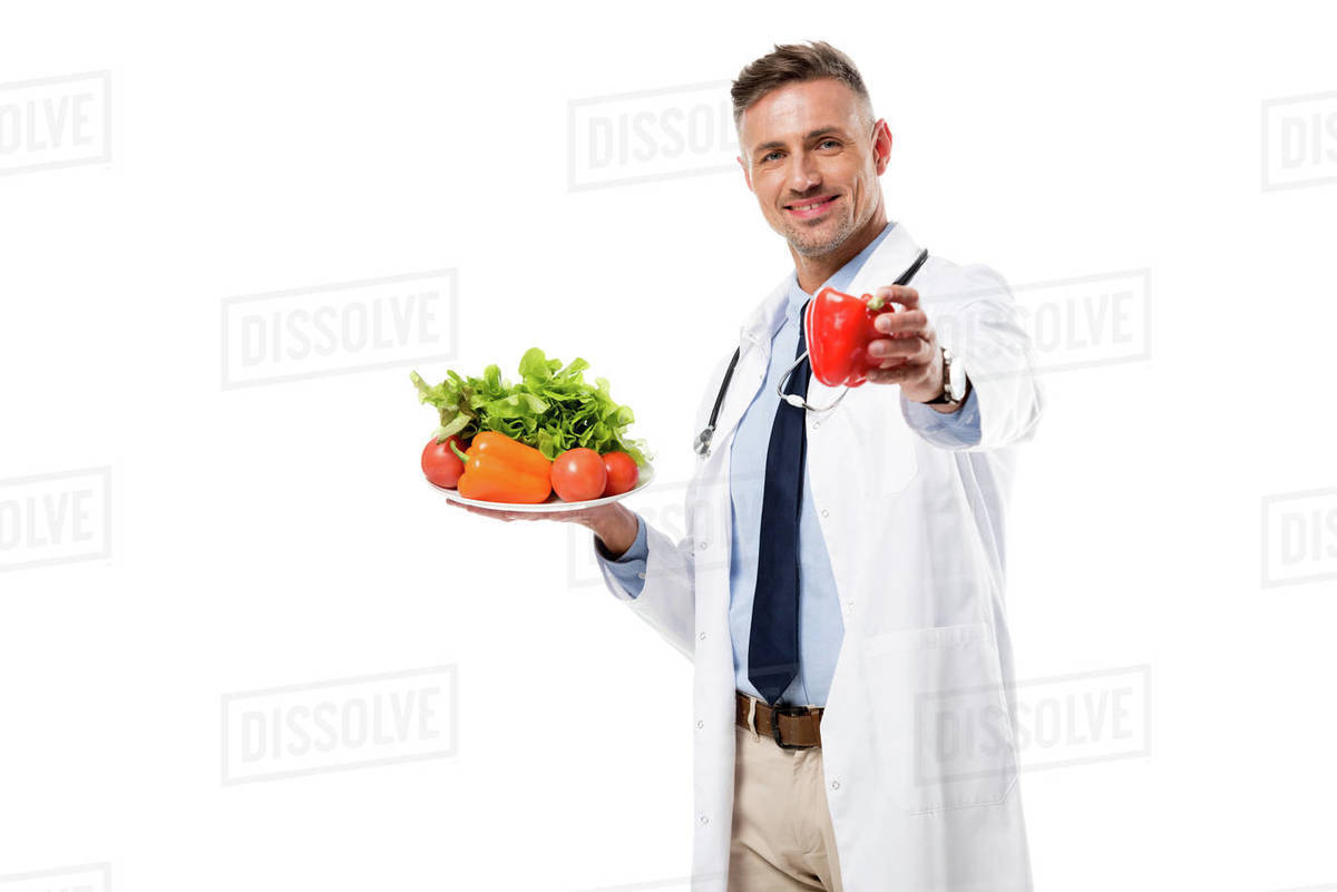 Handsome doctor holding pepper and plate of fresh vegetables isolated ...