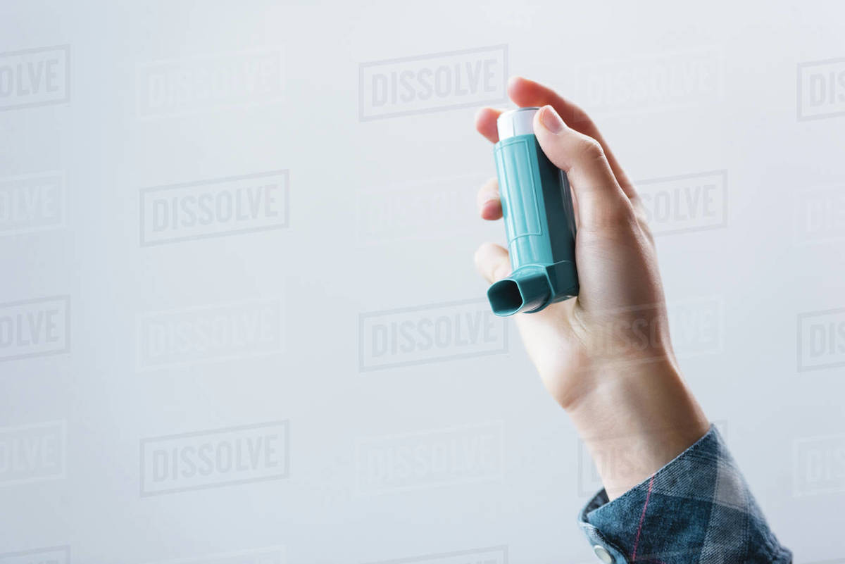 Close-up partial view of young woman holding inhaler isolated on grey ...