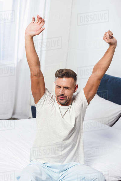 Sleepy man sitting on bed and yawning - Royalty-free Stock Photo | Dissolve