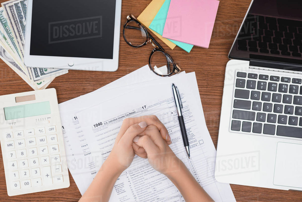 Cropped view of woman with folded hands sitting at desk with tax forms ...