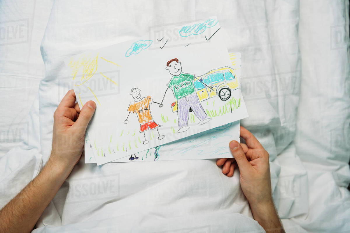 Sick father holding drawings while laying on hospital bed at ward ...