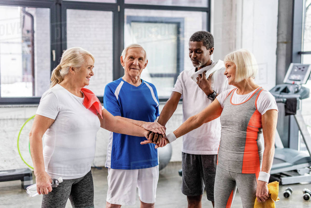 Senior multicultural friends putting hands together at sports hall ...