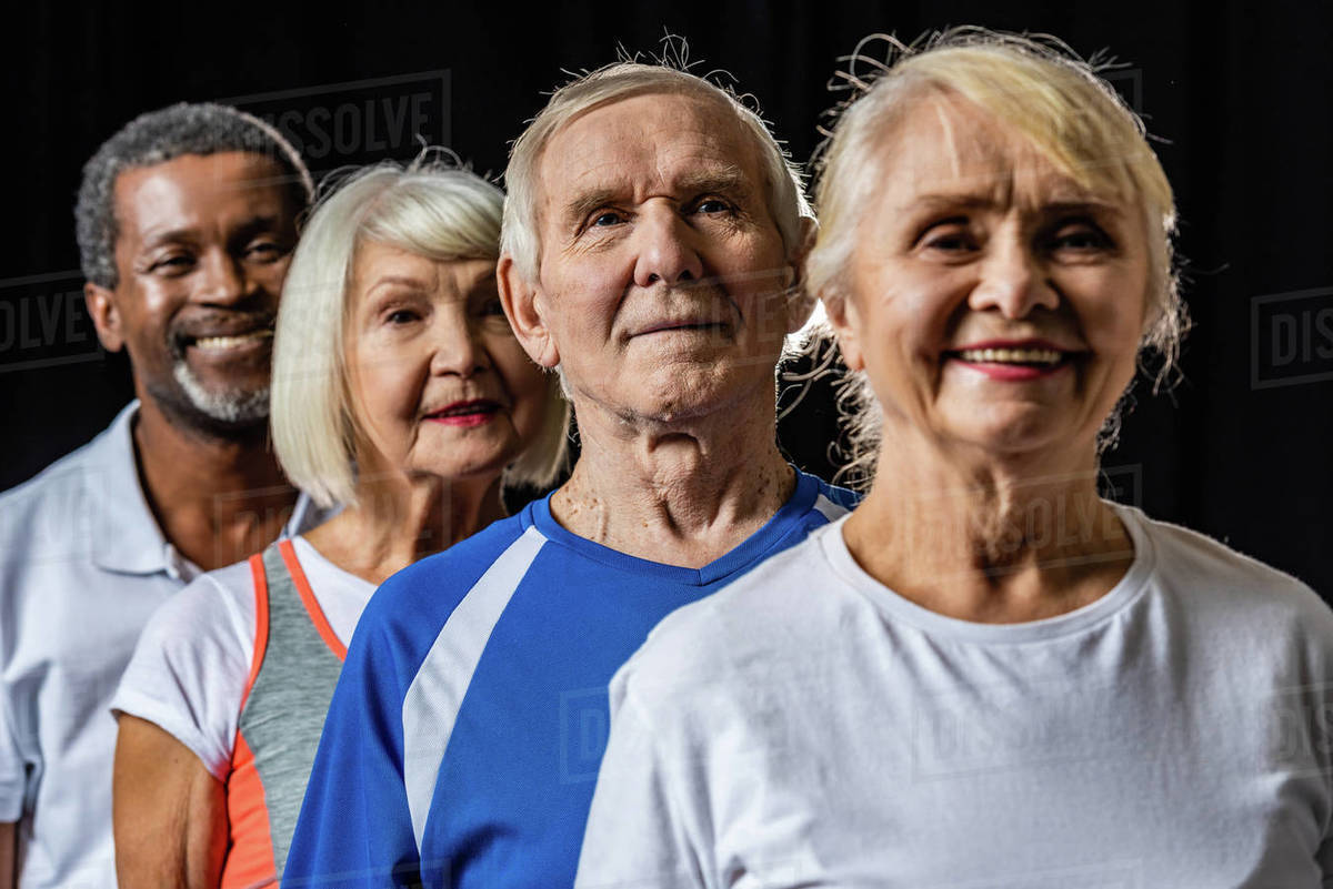 Smiling multicultural senior sportspeople standing isolated on black ...