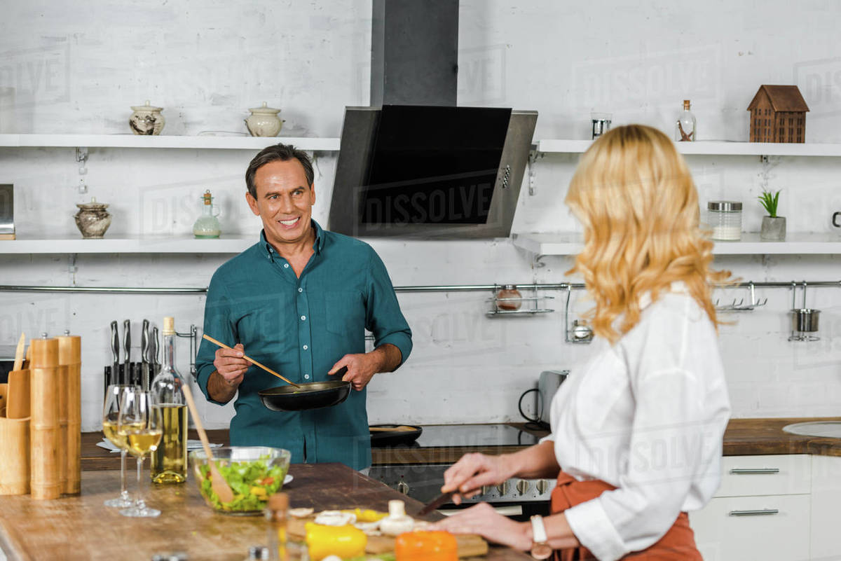 Mature wife and smiling husband cooking together in kitchen - Royalty ...