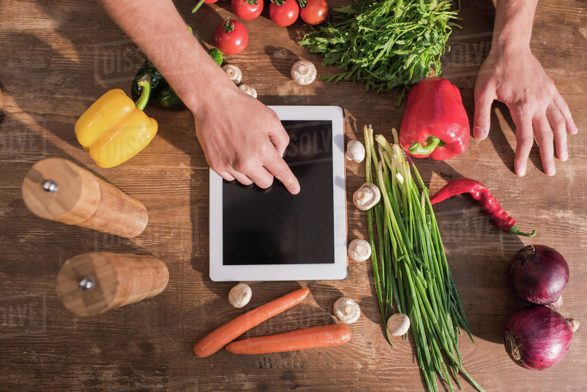 Top view of young man cooking with tablet and pointing at blank screen ...