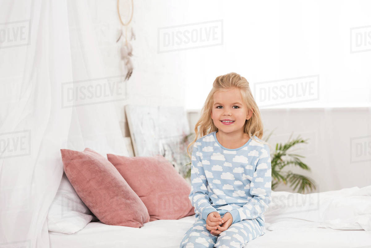 Adorable smiling child sitting on bed in morning - Stock Photo - Dissolve