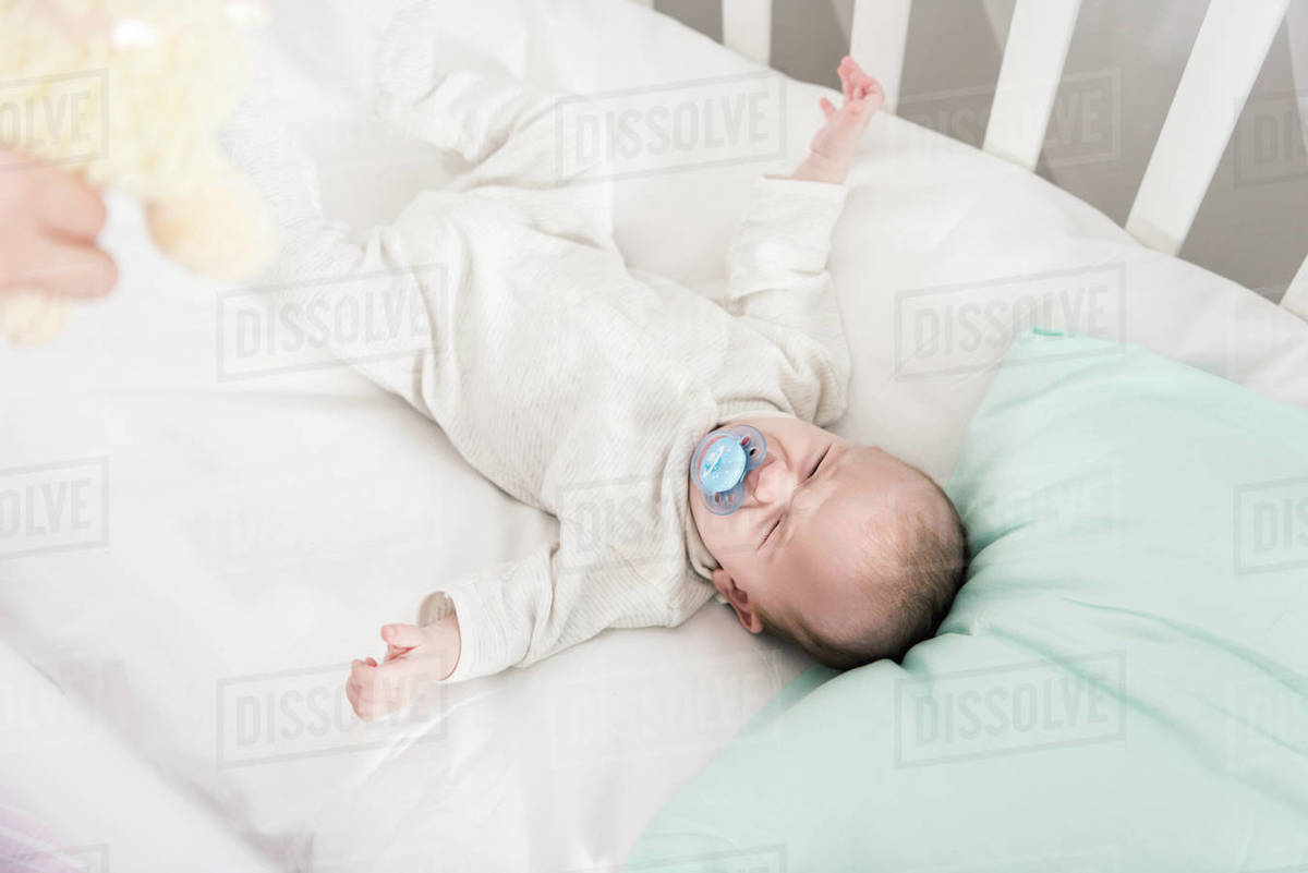 Partial view of parent showing toy to crying baby in crib - Royalty ...