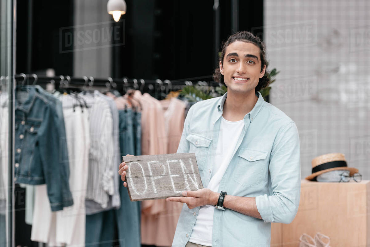 Handsome young shop owner holding open sign and smiling at camera ...
