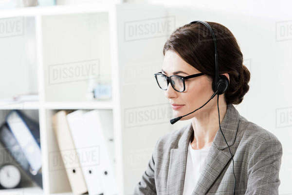 Attractive call center operator in glasses and headset looking away in ...