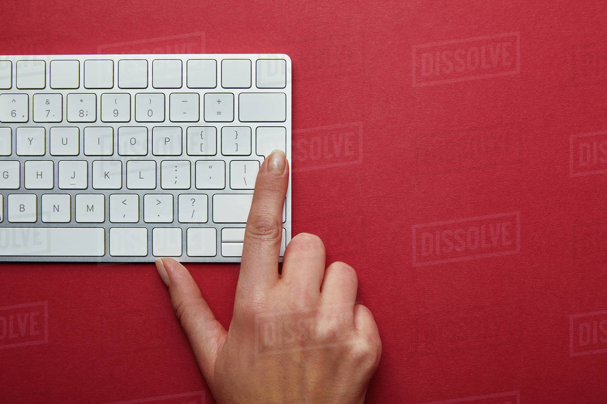 Cropped view of woman pushing button on computer keyboard on red ...
