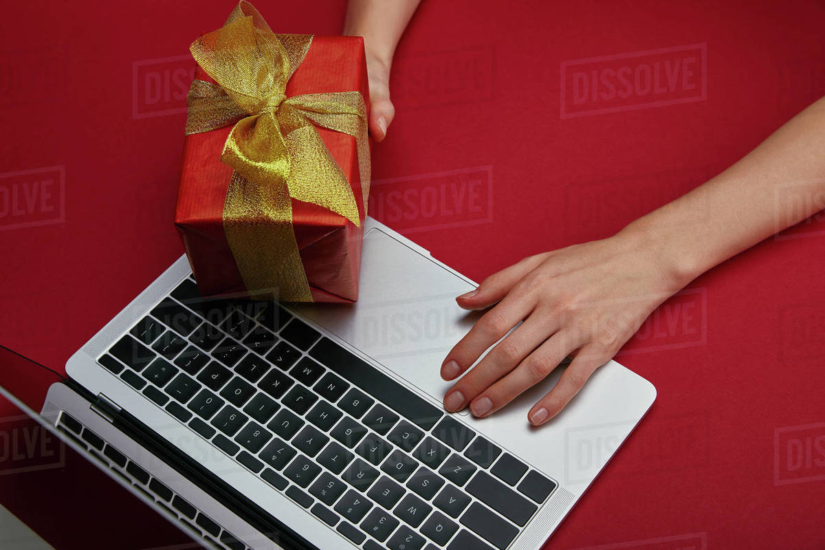 Cropped view of woman holding present near laptop on red background ...