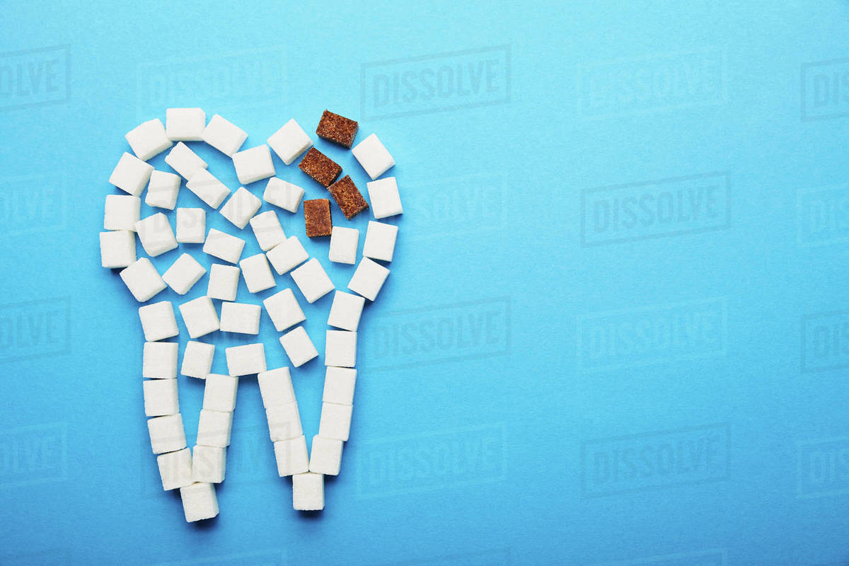 Top view of white and brown sugar cubes arranged in tooth sign on blue ...
