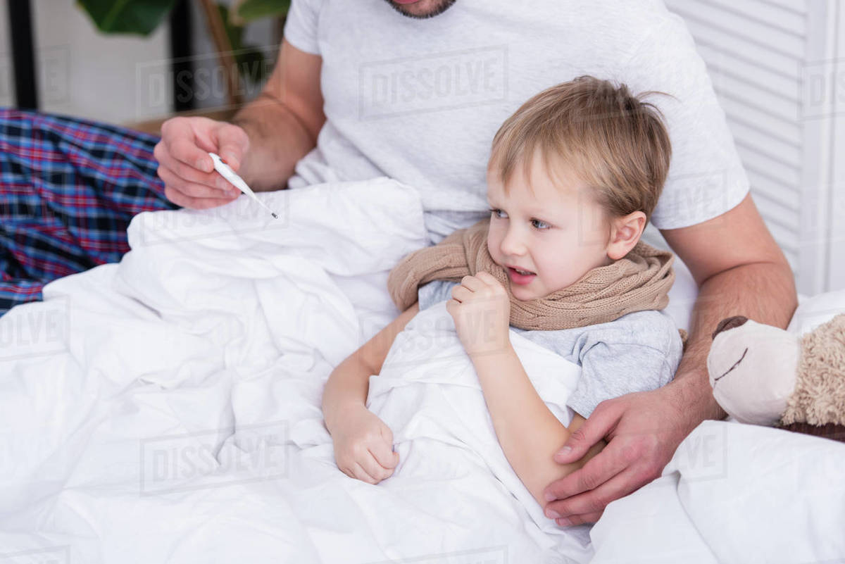 Cropped image of dad hugging sick son in bedroom and checking his ...