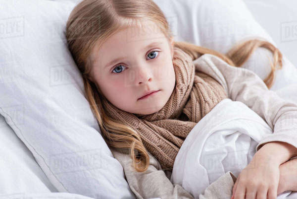 Portrait of sick child with scarf over neck lying in bed at home and ...