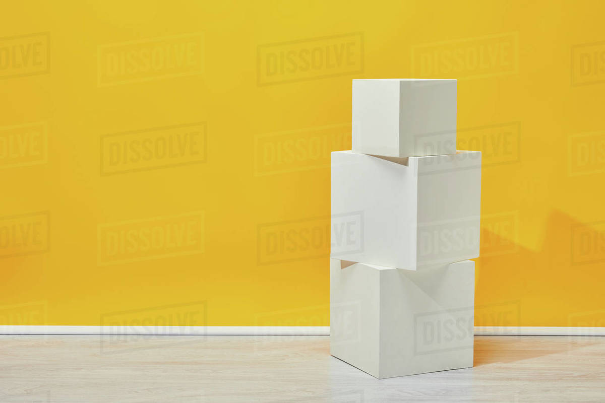 Simple white plaster cubes arranged vertically near yellow wall - Stock ...