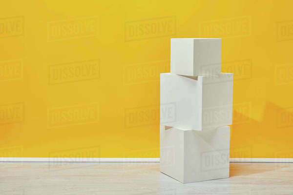 Simple white plaster cubes arranged vertically near yellow wall ...