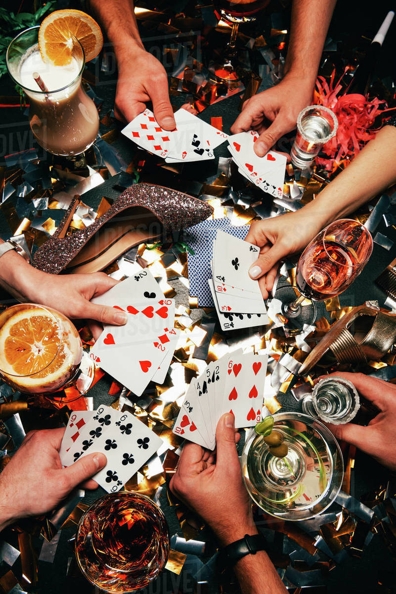 Cropped shot of friends with alcoholic cocktails playing poker at table ...