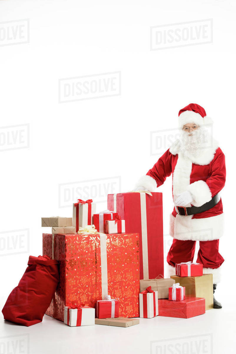 Happy Santa Claus standing with a pile of Christmas gifts isolated on ...
