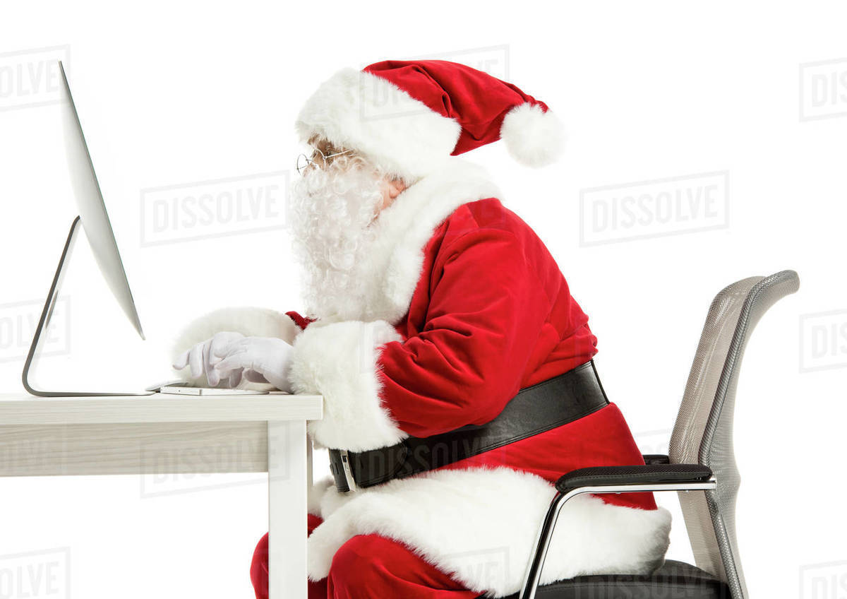 Side view of Santa Claus sitting at the desk and working on computer ...