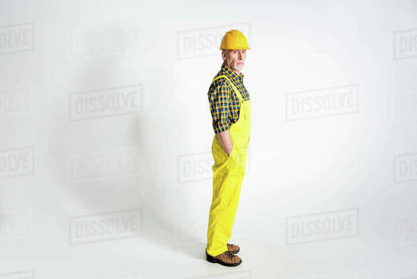 Full length portrait of mature workman in hard hat looking at camera ...
