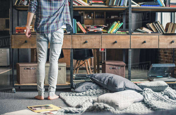Back view of young barefoot man choosing books from bookshelves at home ...