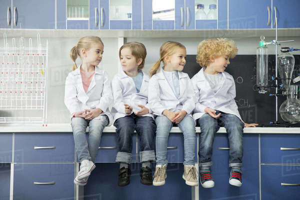 Schoolchildren in lab coats sitting together in chemical laboratory ...