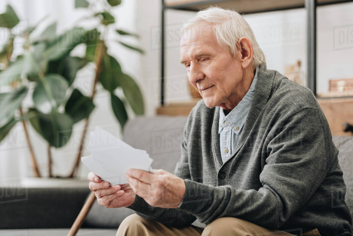 Happy pensioner with grey hair looking at photos in living room ...