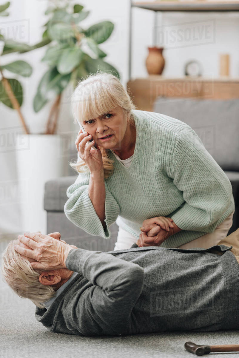 Senior woman helping old man with walking stick and looking at camera ...