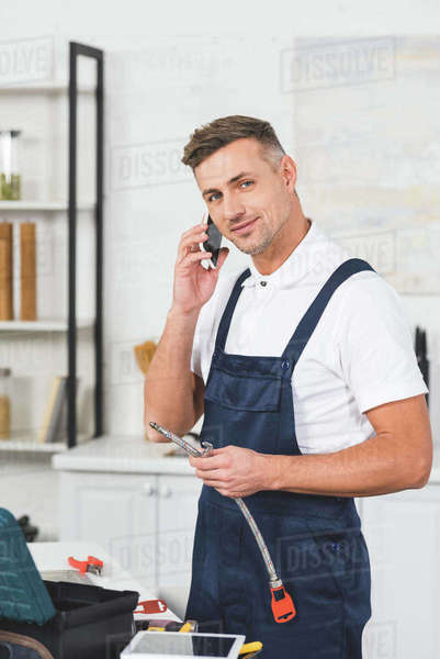 Smiling adult repairman holding pipe for kitchen faucet repairing and ...
