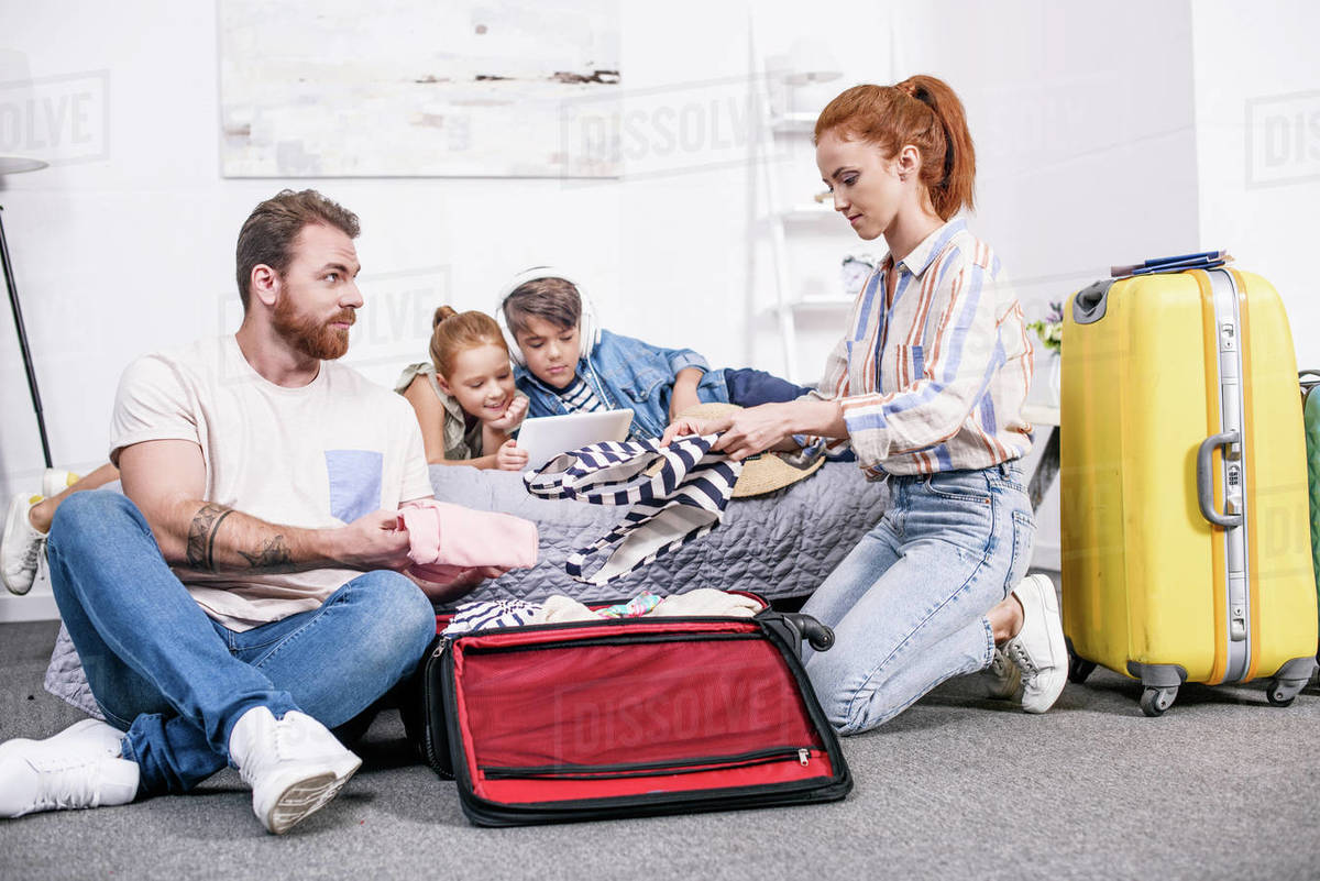 Happy family packing luggage for trip in bedroom - Stock Photo - Dissolve