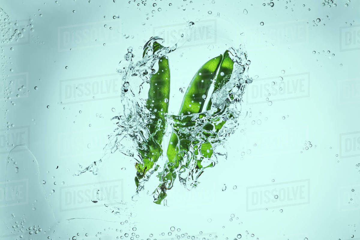 Fresh green peas floating in water with splash on blue - Royalty-free ...