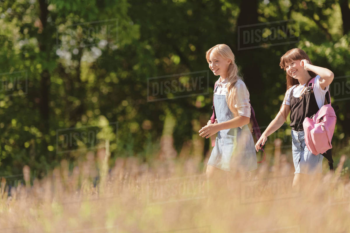 Side view of beautiful smiling teenage girls with backpacks walking in ...