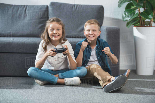 Smiling children playing video game with joystick at home - Royalty ...