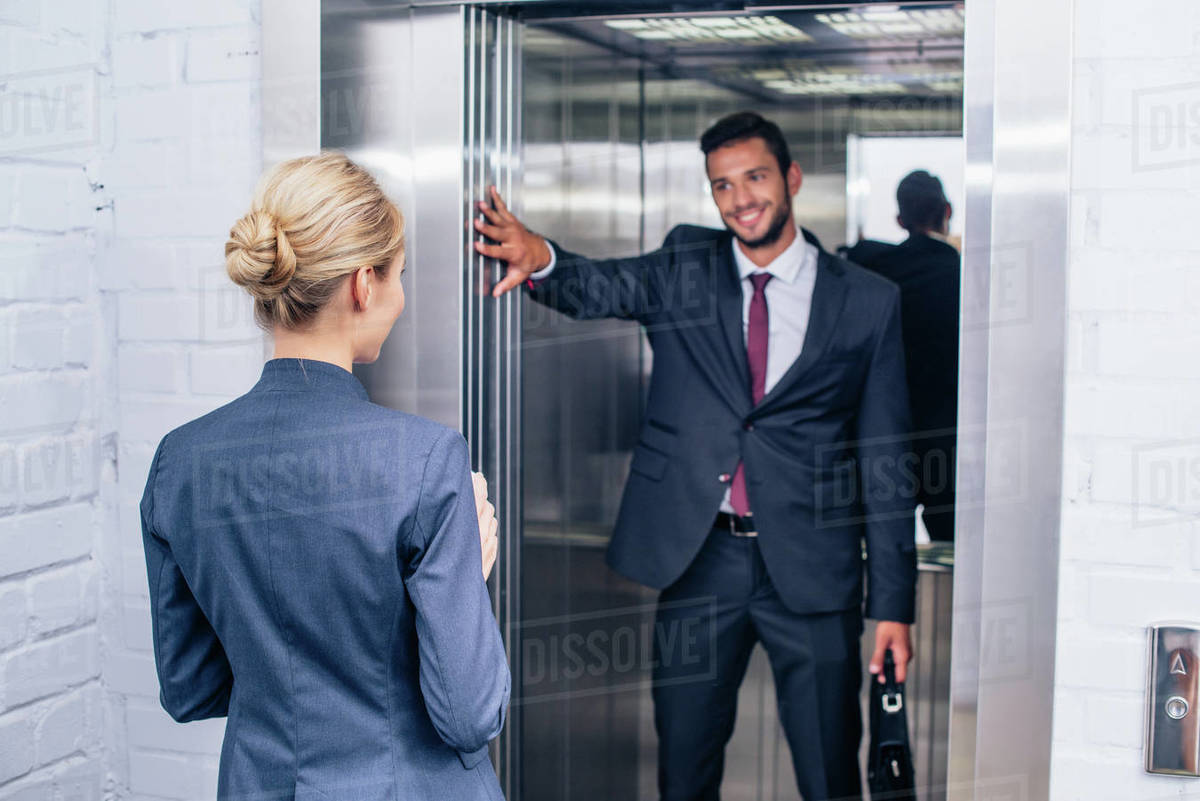 Smiling handsome businessman holding elevator door for woman - Royalty ...