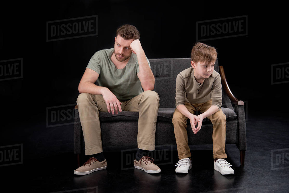 Upset father and son sitting on sofa and looking away, family problems ...