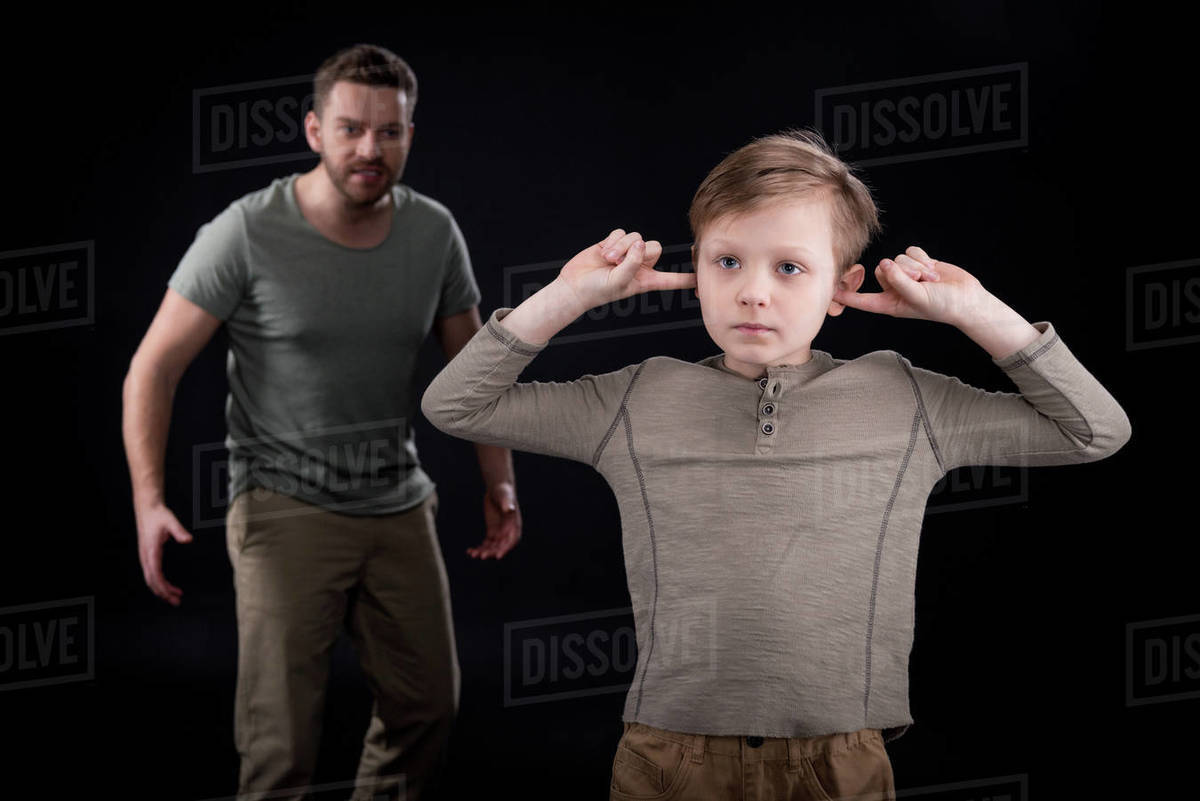 Angry father looking at son standing and closing ears with fingers ...