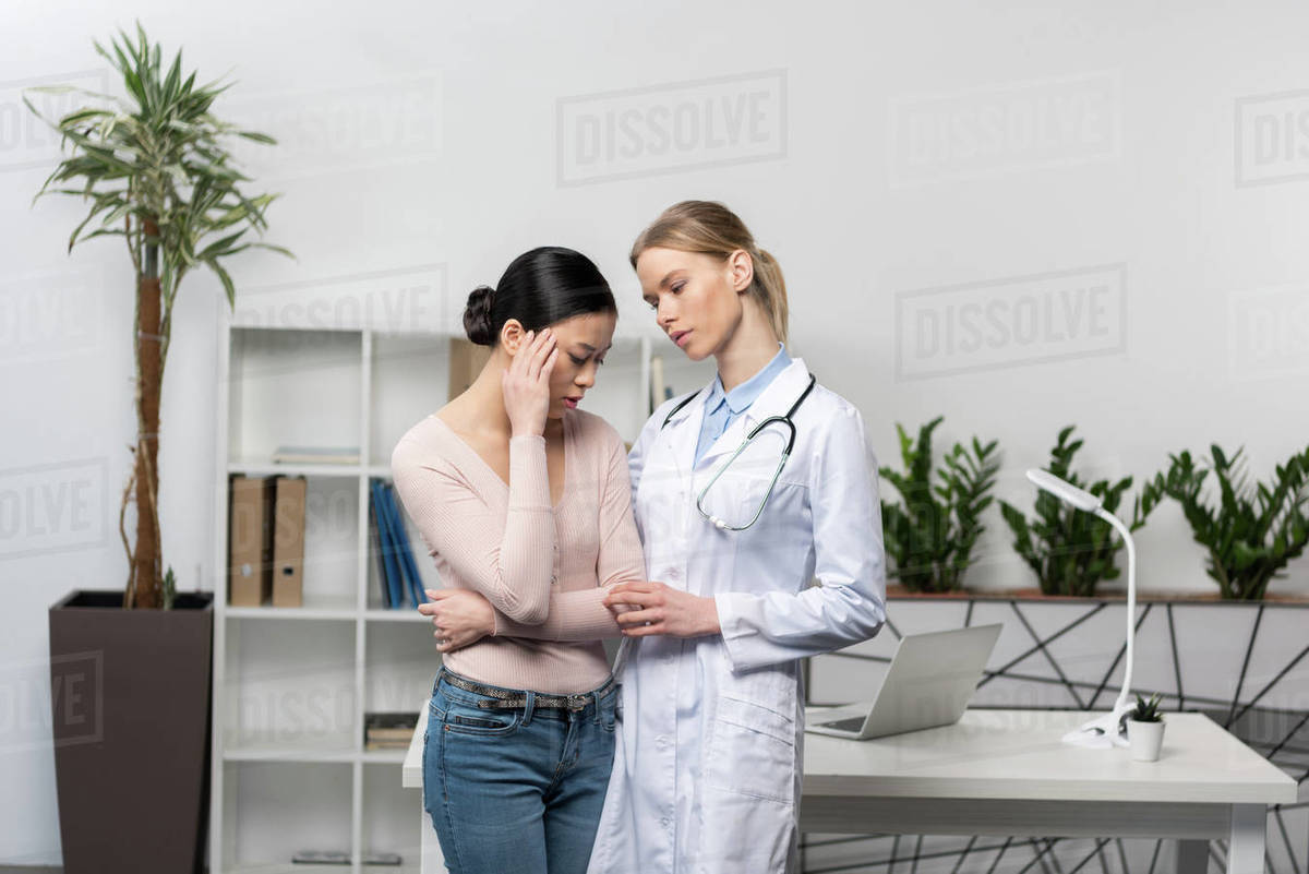 Young doctor with stethoscope talking with upset patient suffering from ...