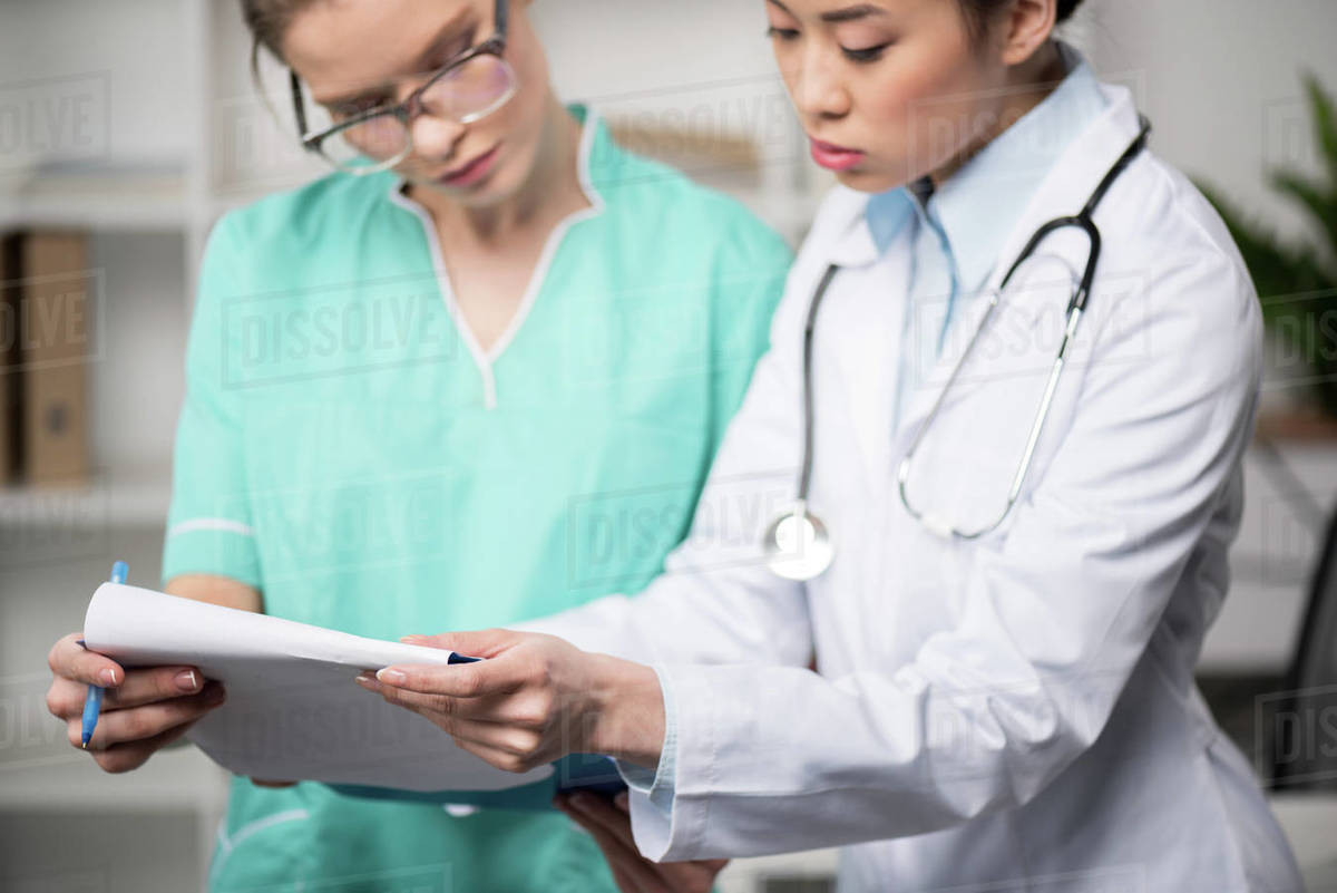 Portrait of focused doctors looking at clipboard together at clinic ...