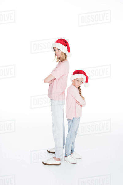 Grumpy mother and little daughter in Santa hats posing with arms ...