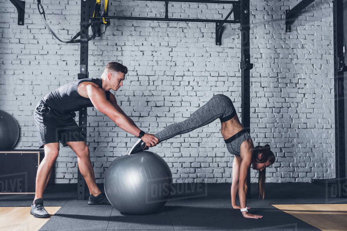 Side view of trainer holding sportive woman while she working out on ...