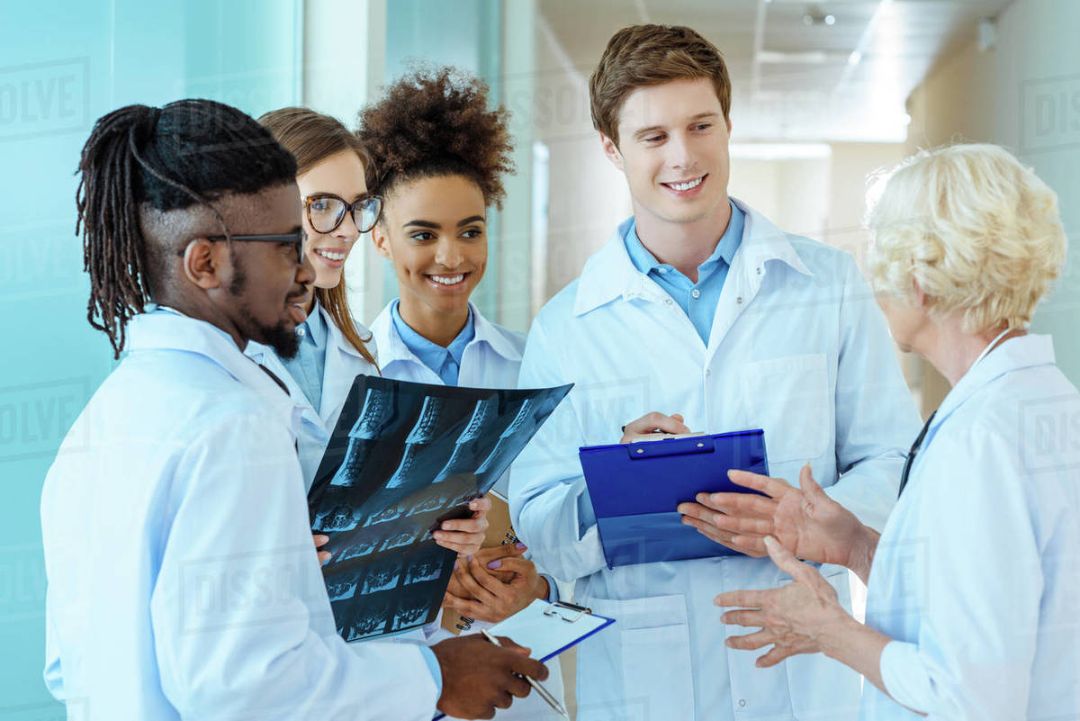 A multiracial group of young medical interns listening to a elder ...