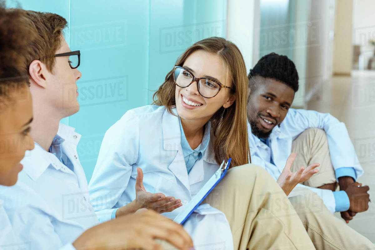 Four young medical interns sitting on floor in hospital corridor ...