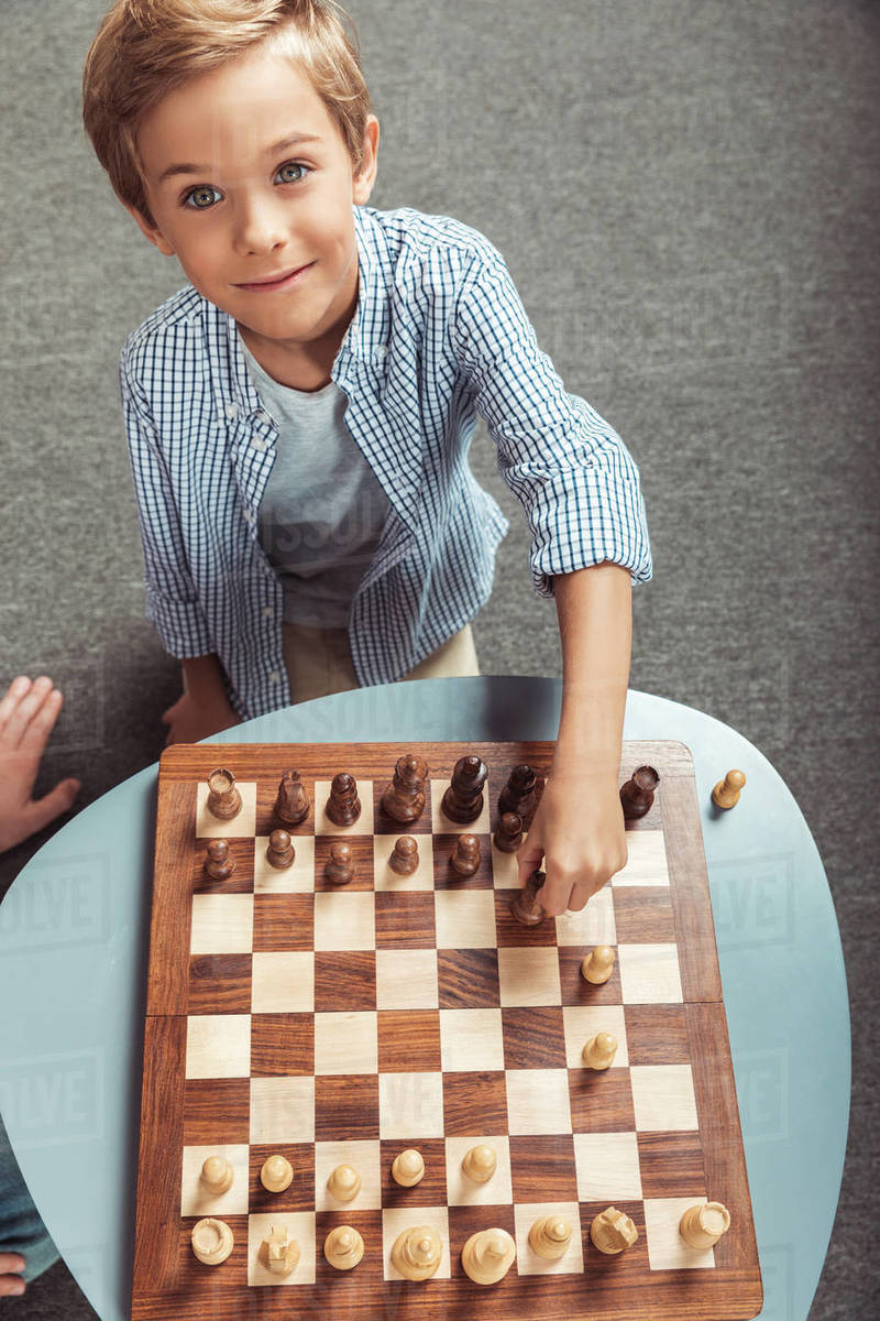 High angle view of cute little boy playing chess and smiling at camera ...