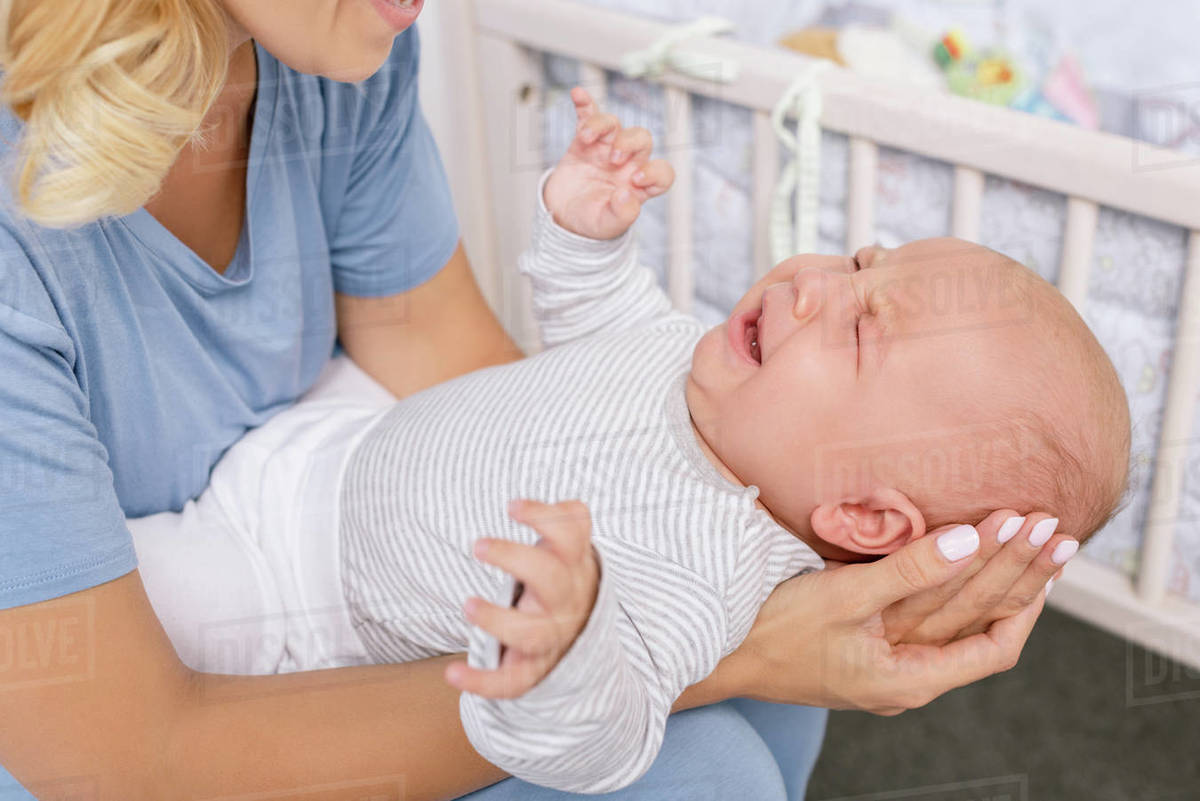 Cropped shot of mother holding crying baby in hands at home - Royalty ...