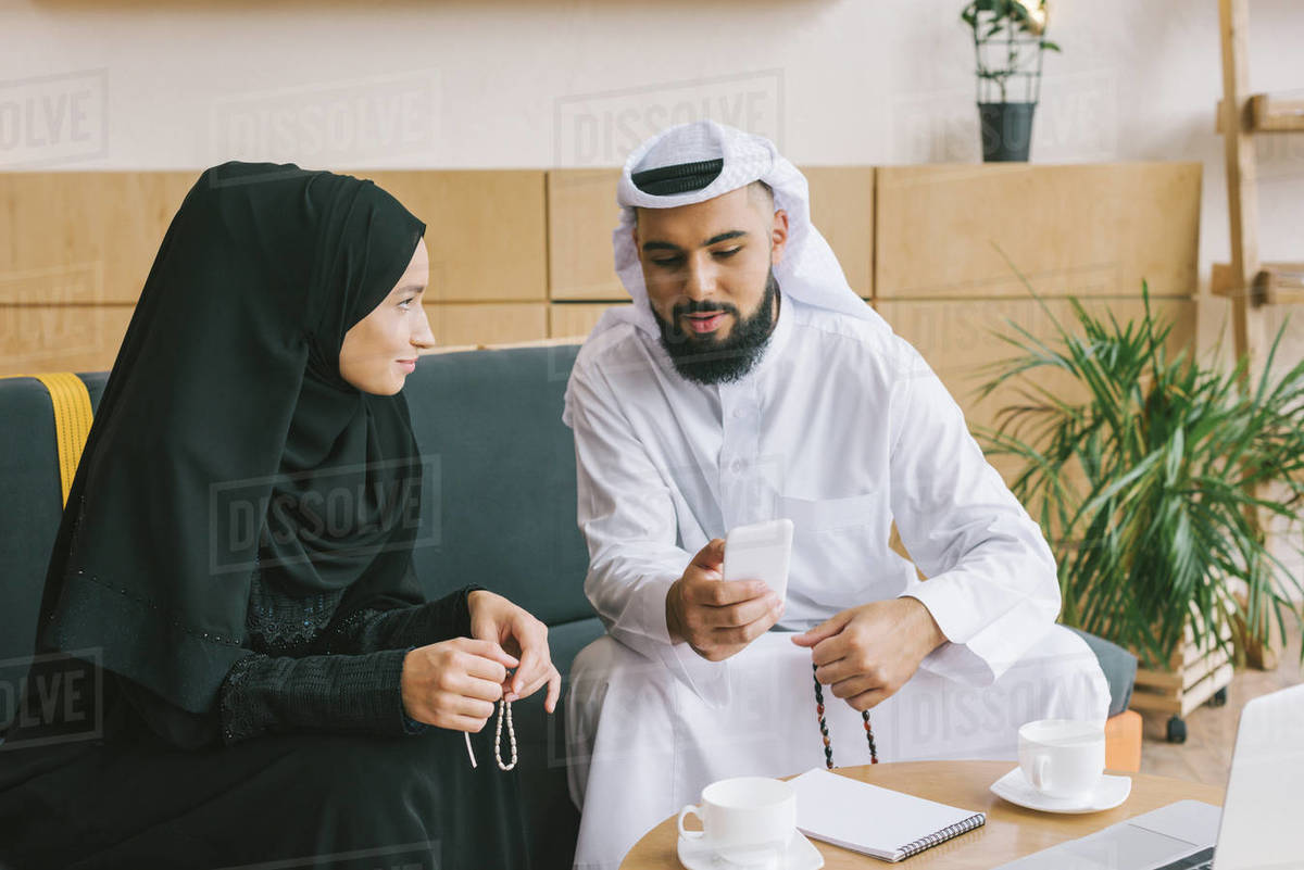 handsome muslim man showing smartphone to woman - Stock Photo - Dissolve