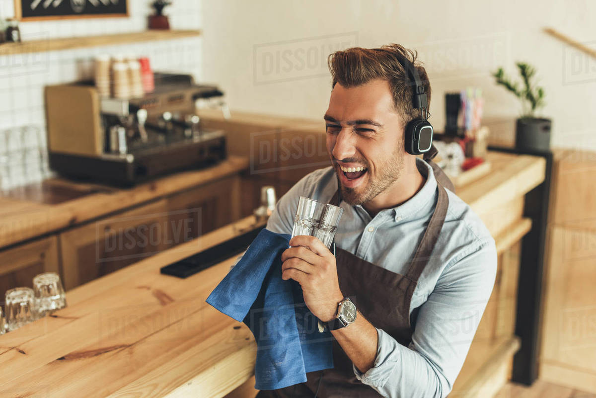 Worker in headphones pretending singing while cleaning glassware in ...