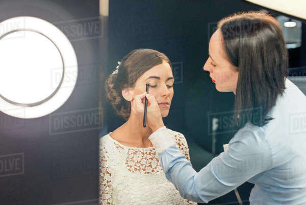 Side view of focused makeup artist applying eye shadows on models face ...